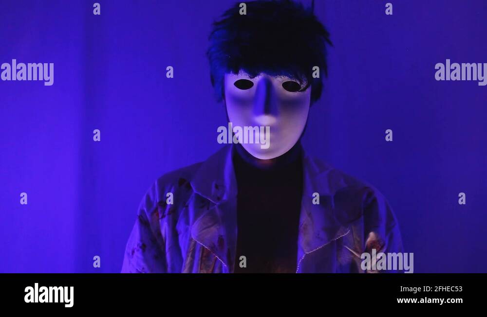 A person wearing a white creepy mask and a bloody doctor suit, in a ...