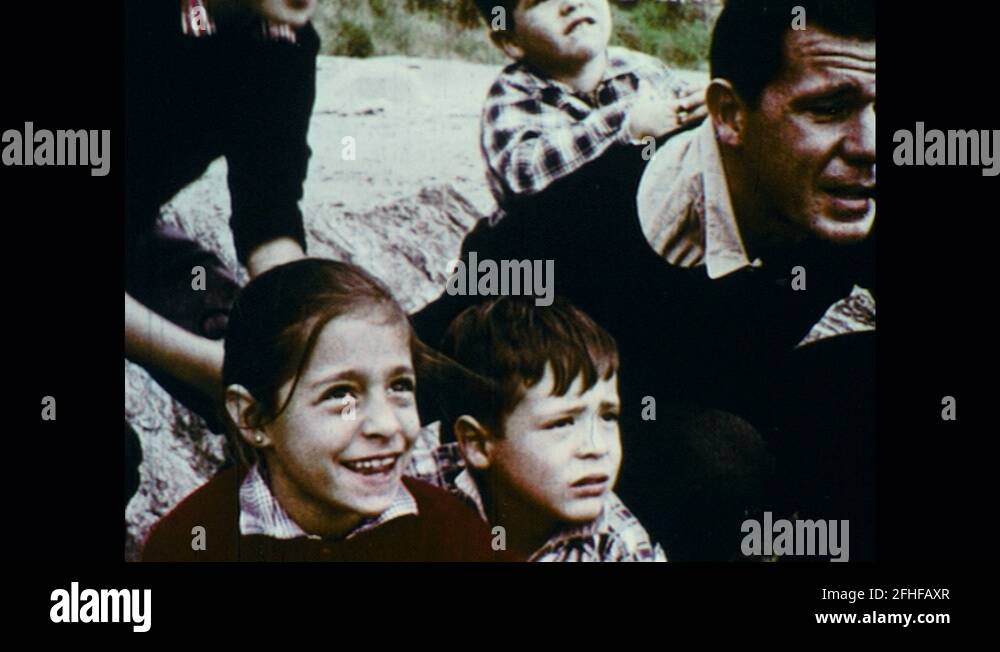 1960s: Kids crouch on beach rocks next to man with pipe. Group of ...