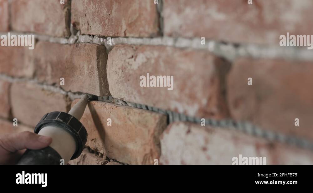 Slow motion pan closeup of worker filling seam between bricks with ...