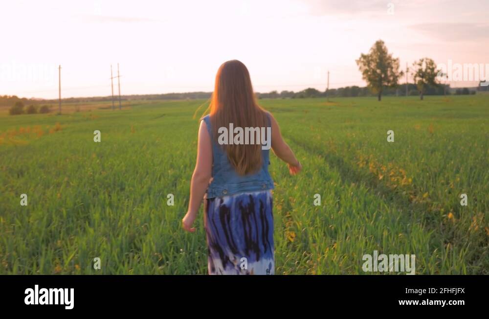 Young girl walking on the field at sunset and showing the middle finger ...