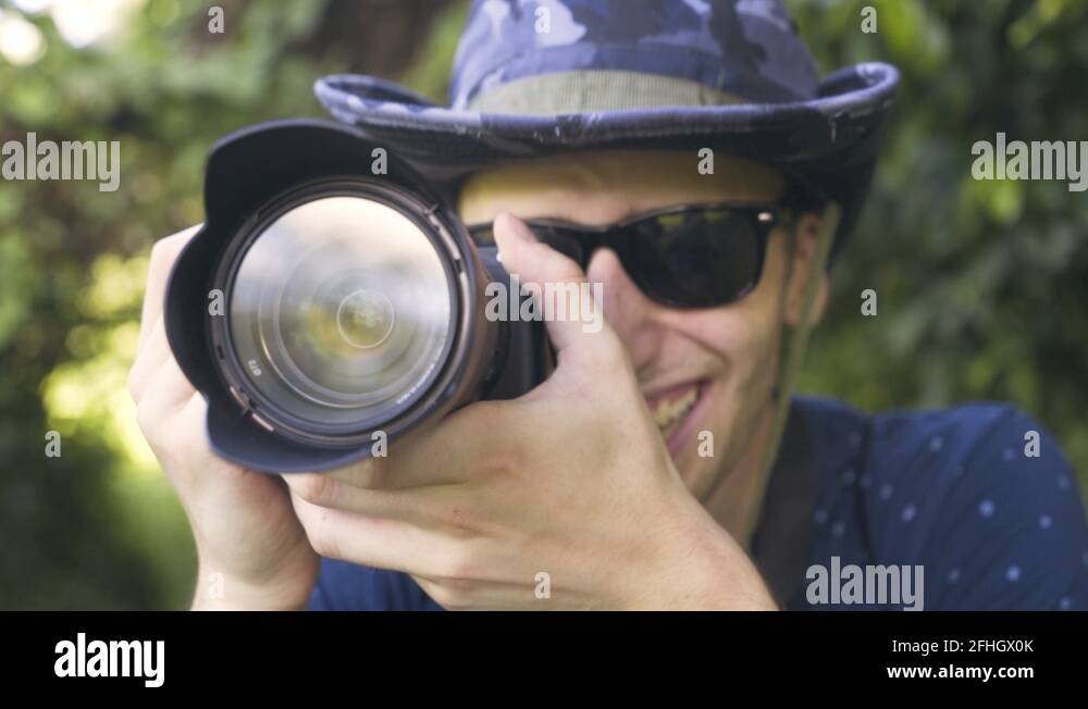 Young millennial photographer lifts the camera to his eye and smiles ...