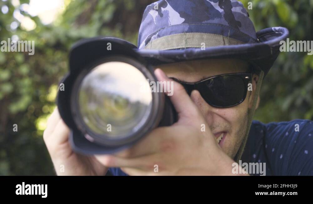 Young millennial photographer lifts the camera to his eye and smiles ...