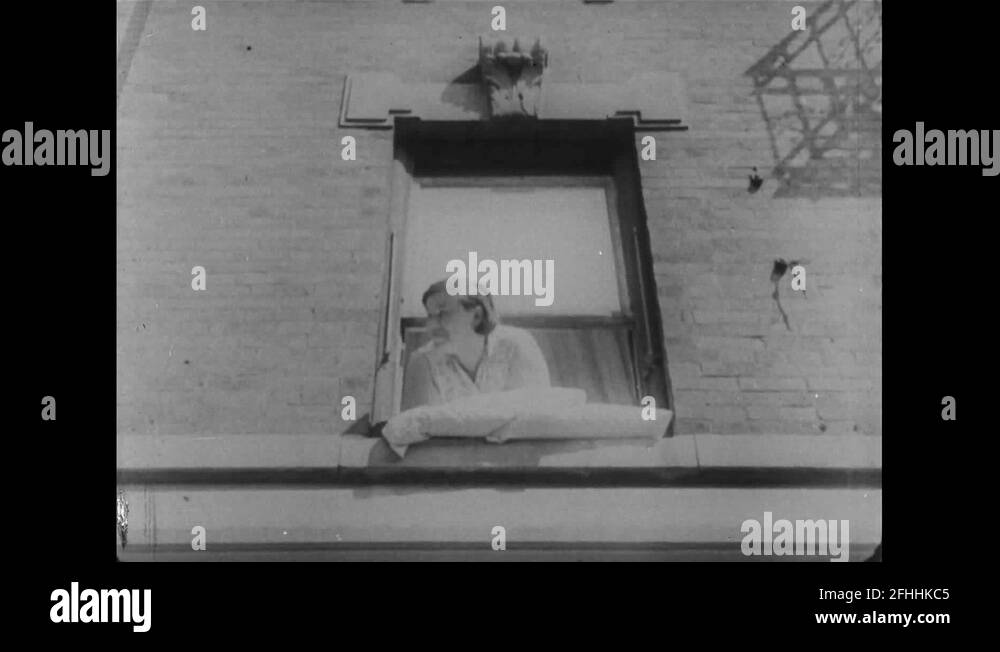 1930s: Woman talking from window. Hands wave sheet from window. Woman ...