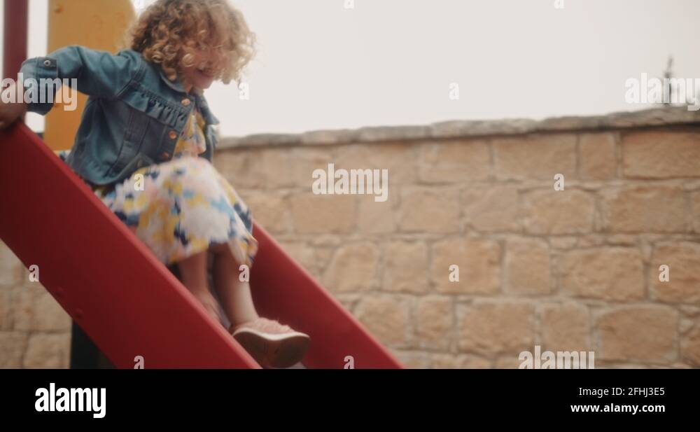 Girl having fun on kindergarten playground slide during school recess ...