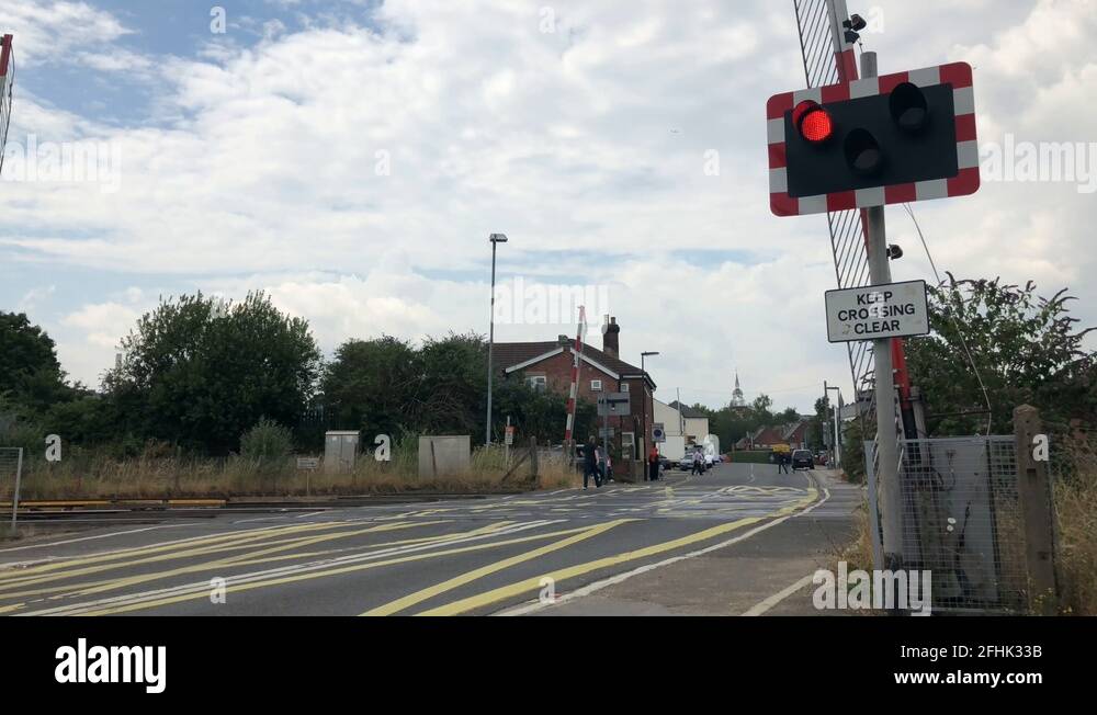Level crossing signal with barriers lowering and people walking across ...