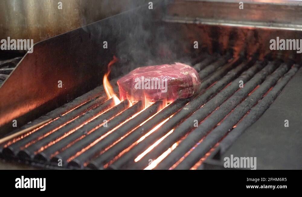 Steak being cooked on a grill as flames shoot up beside the meat Stock ...