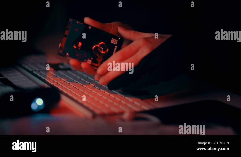Hacker hands holding a hard drive by a keyboard, slowlying it from one ...