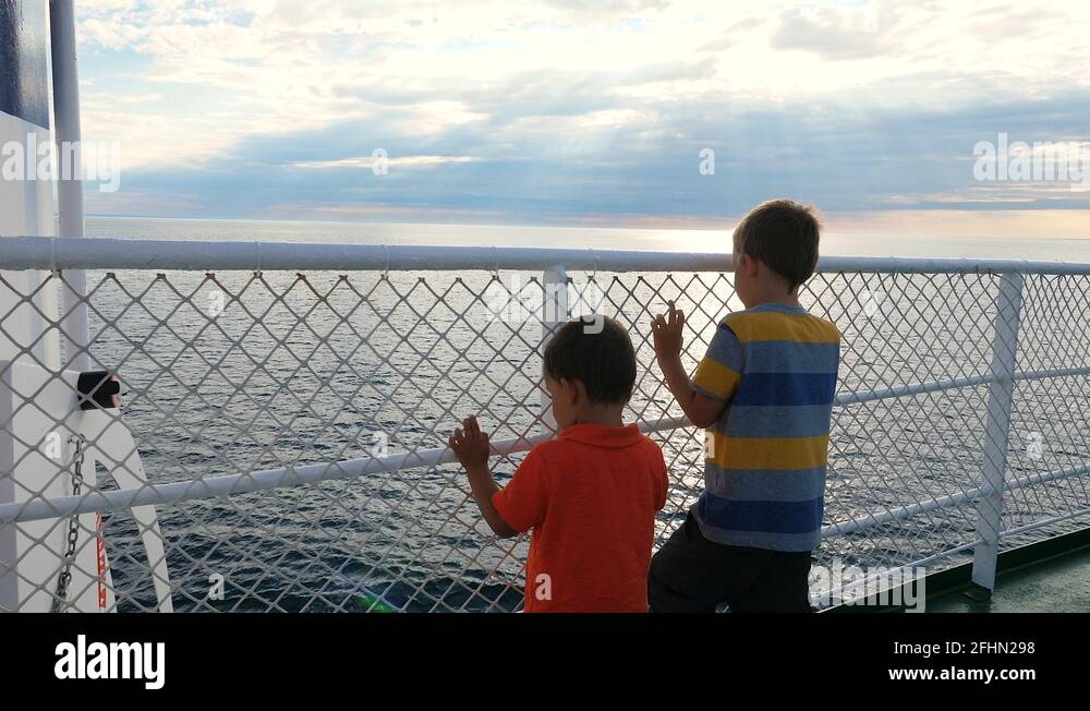 Boys look out over an ocean sunset while traveling on a large boat ...