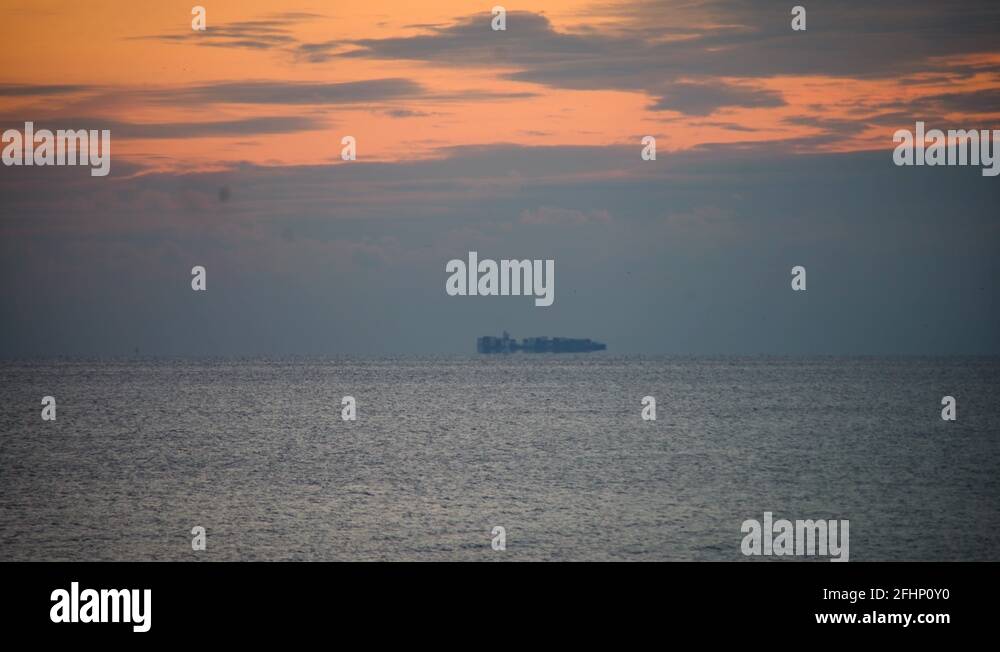During sunrise theres a mirage effect on a cargo ship far in the ...
