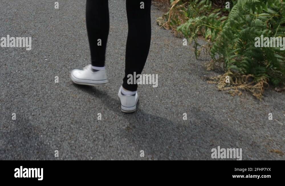 Women's foot steps from behind strolling along tarmac path with ...
