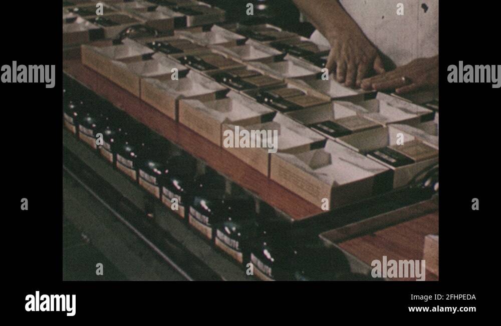 1950s: Factory. Women fill boxes on assembly line. Hand stamps label on ...