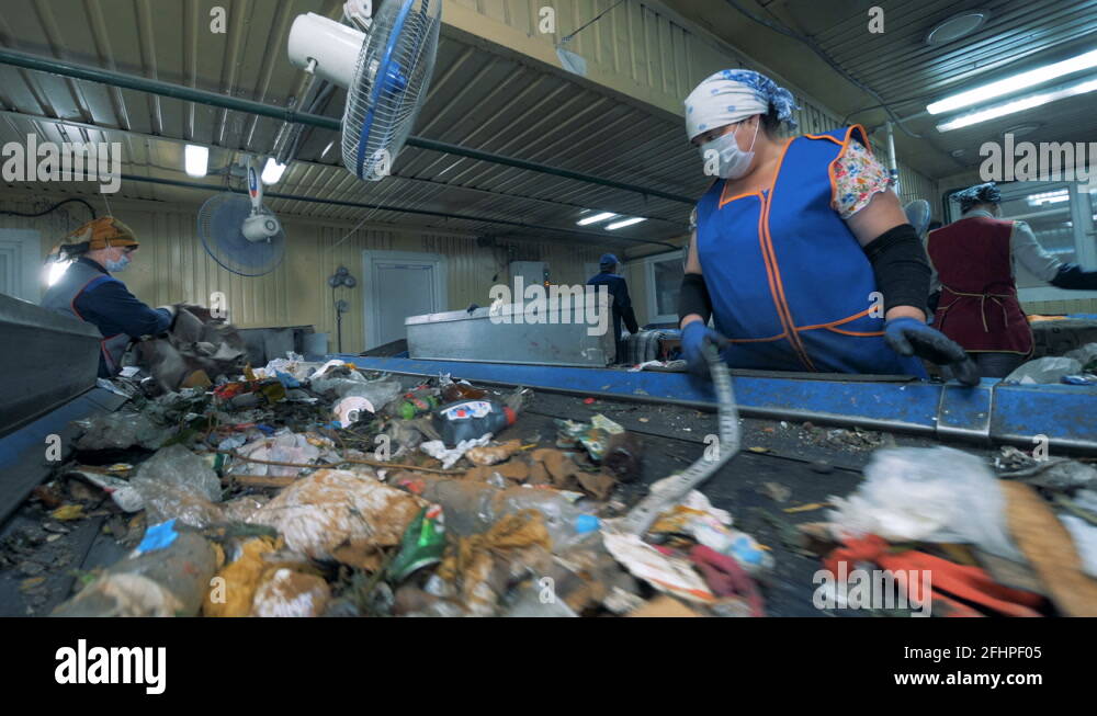 People are sorting garbage which goes on conveyors in a recycling plant ...