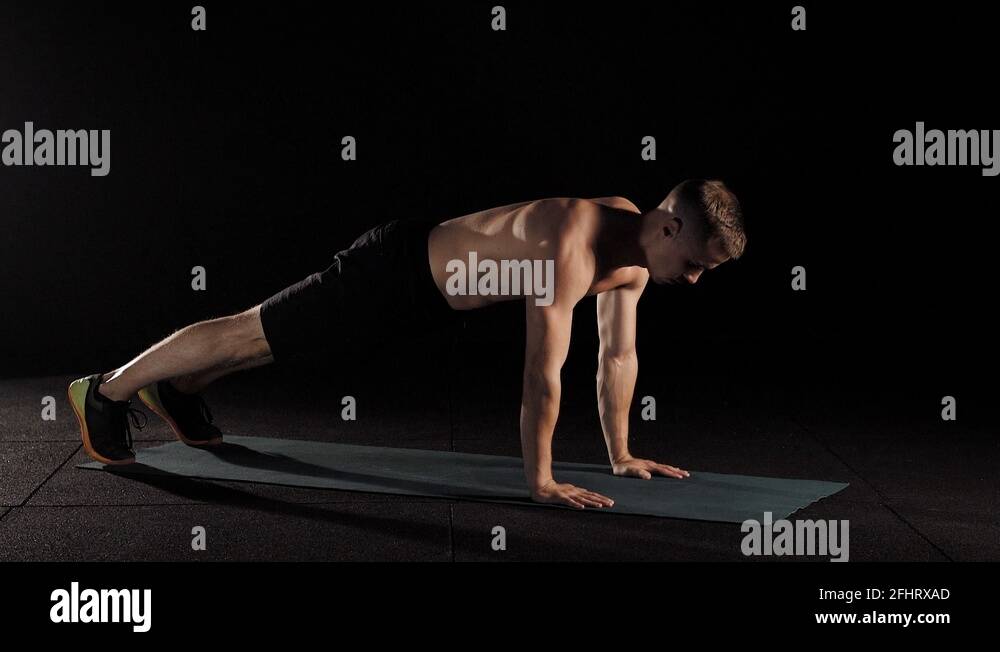 Muscular male athlete model doing pushups on a mat in a professional ...