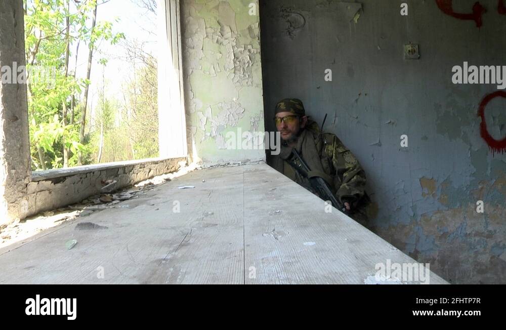 Soldier in military uniform with a weapon is in position in a destroyed ...