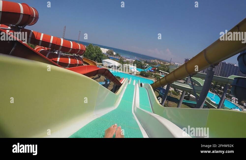 Two happy female friends roll in parallel on a slide in water park ...