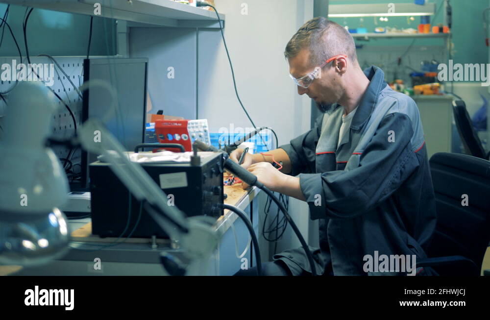 Workshop with a male employee soldering a circuit with artificial hands ...