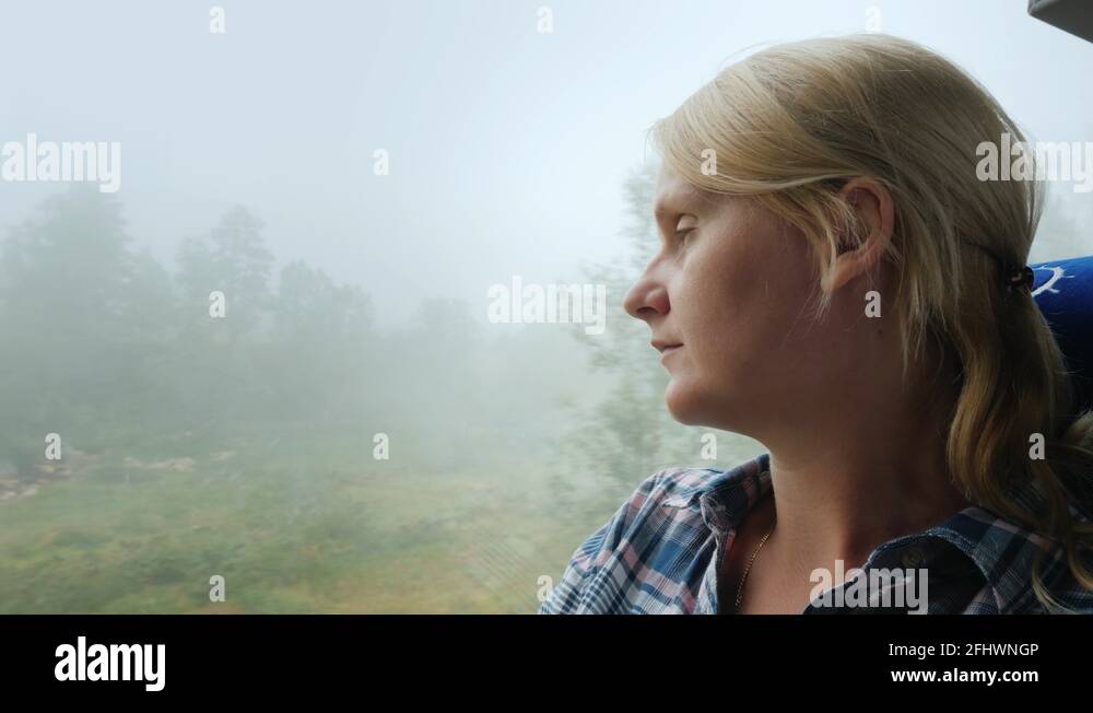 A woman looks out the window of a bus to a forest covered with thick ...
