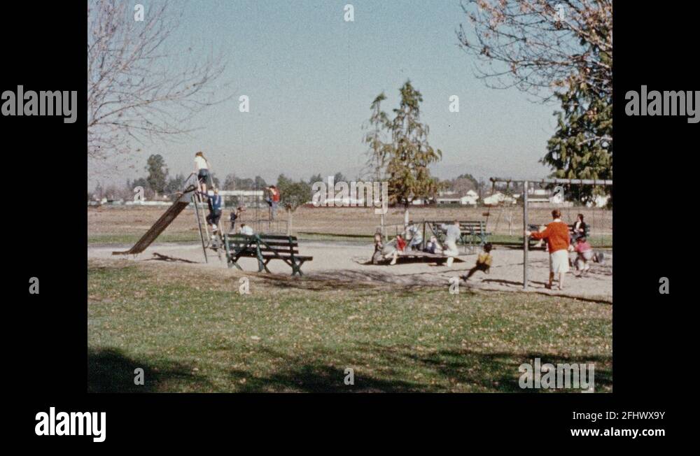 1960s: boys and girls play on playground equipment at park. boys spin ...