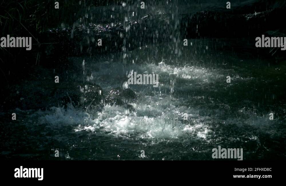 Tilt up of jungle waterfall splashing onto a log over a river in slow ...