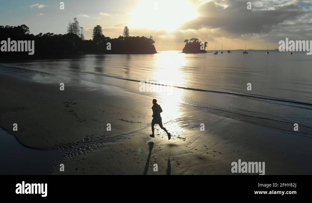 Cinematic aerial tracking shot of silhouetted young man running on a ...