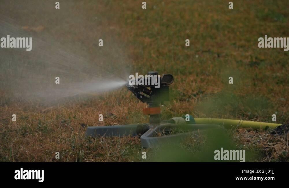 The lawn mower sprays water over the green grass. Lawn Irrigation ...