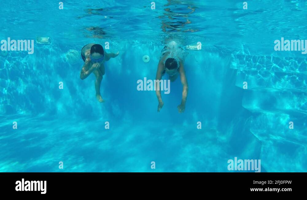 Energetic boys swimming underwater and pushing off the wall in a pool ...
