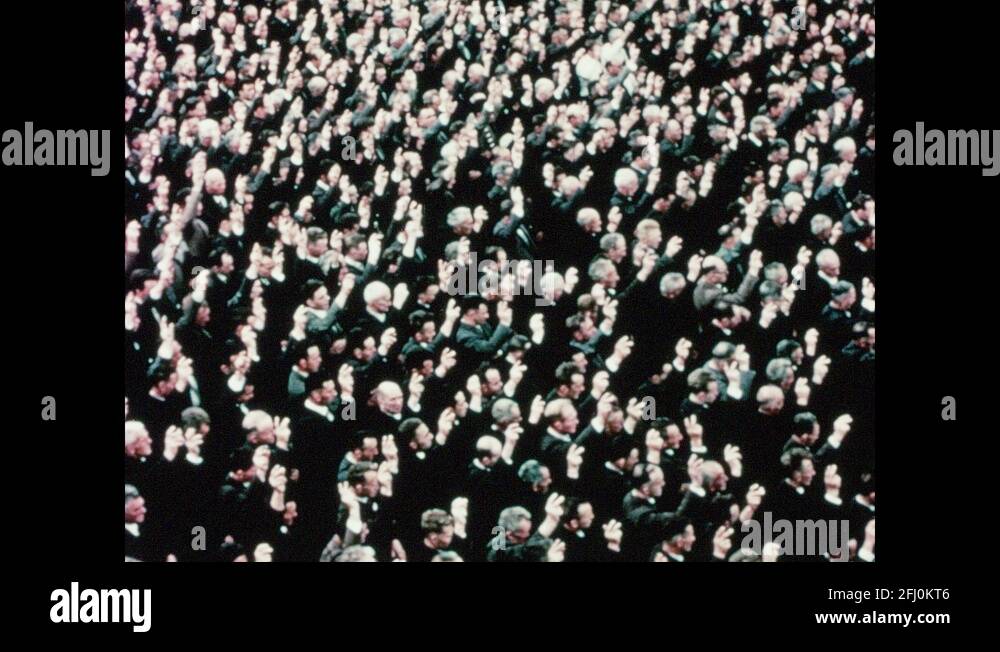 1960s: Swiss men stand and raise hand. crowd of guys, women, boys and ...