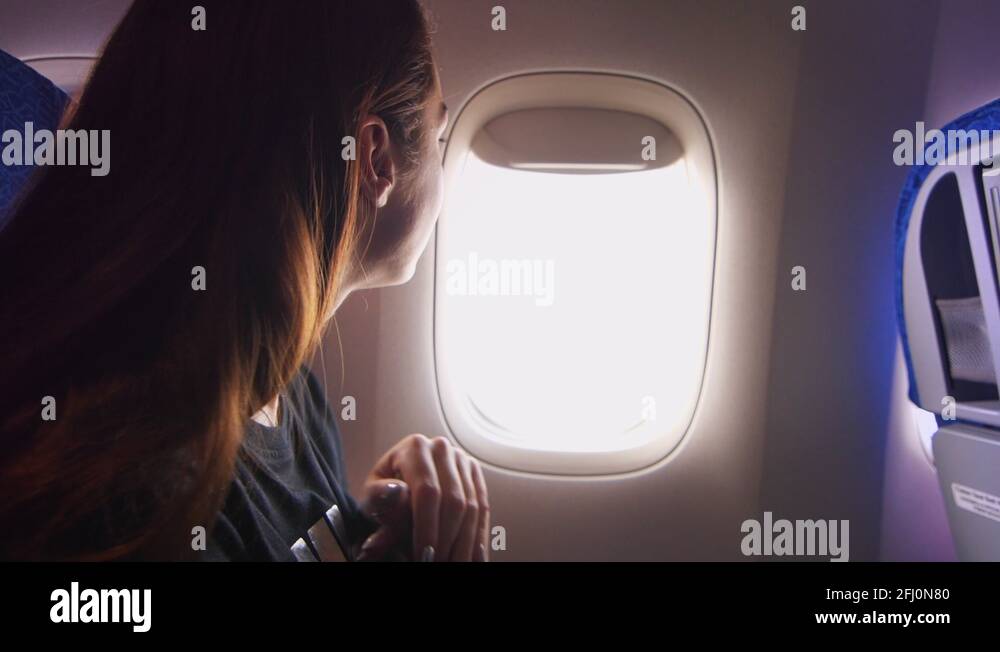 Beautiful girl looking out window of airplane during flight in slow ...