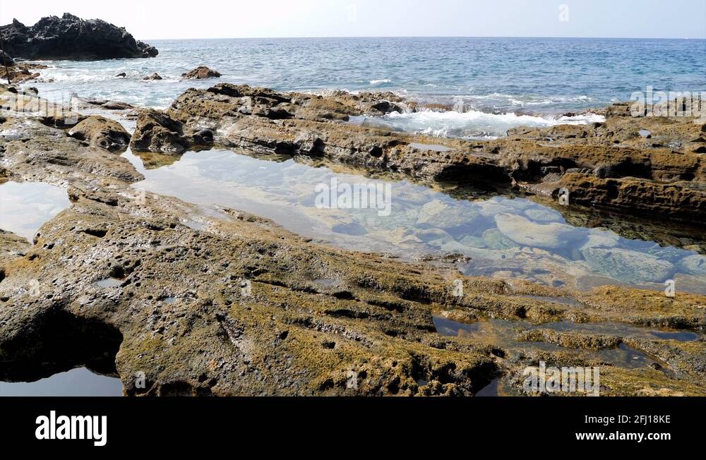Woman sitting on the rocks by a sea water puddle and the ocean in the ...