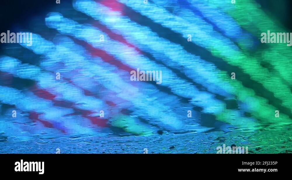 Neon Reflections glow in a puddle of water as a Young Woman walks ...