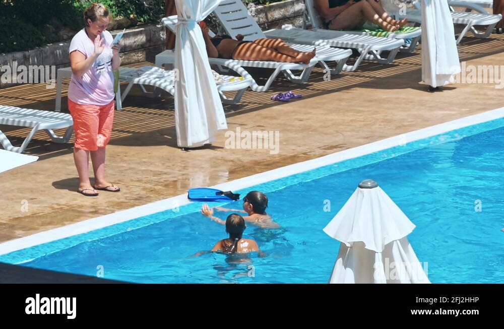 People sitting by the poolside of a resort swimming pool during summer ...