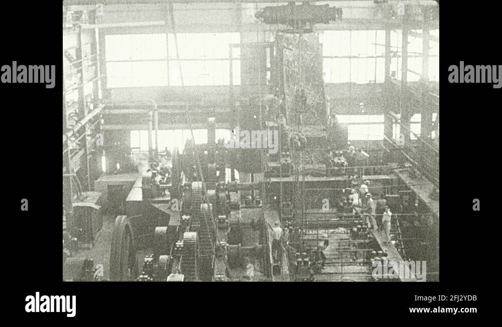 1930s: Inside factory, with large wheels turning and conveyor belt ...