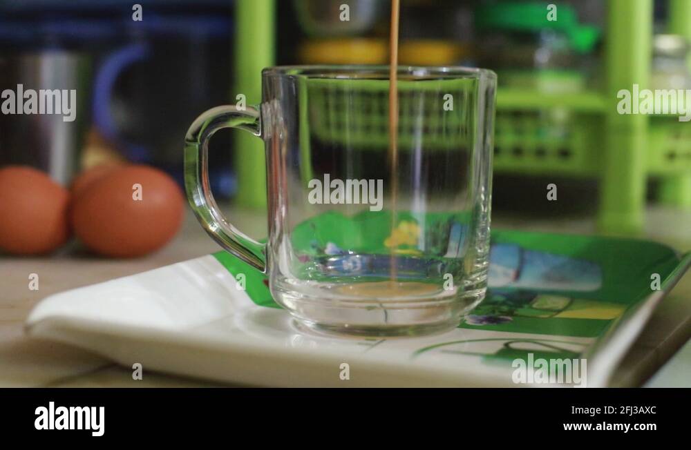 Pouring chai tea, also known as milk tea into a clear glass cup that is ...