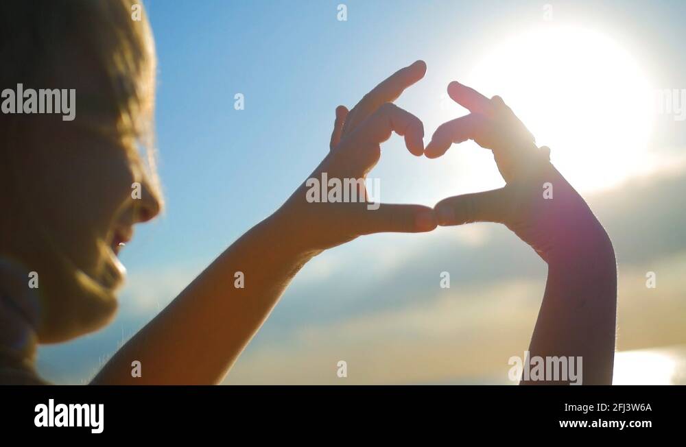 Hands forming a heart shape with sunset silhouette. Ocean sun shining ...