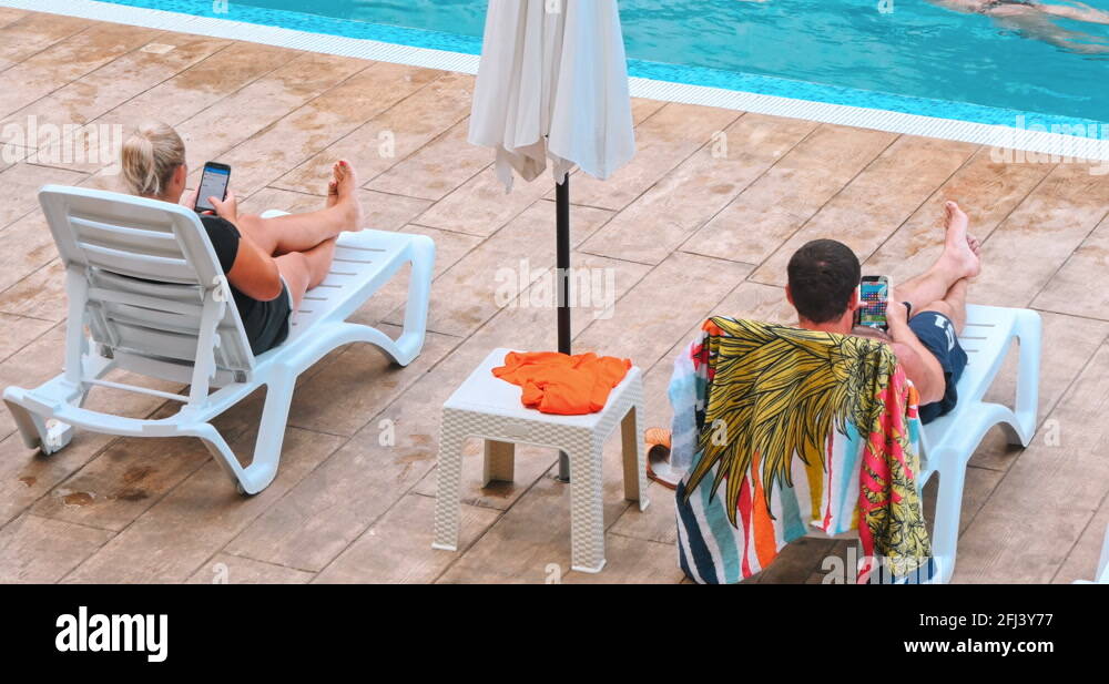 People sitting by the poolside of a resort swimming pool during summer ...