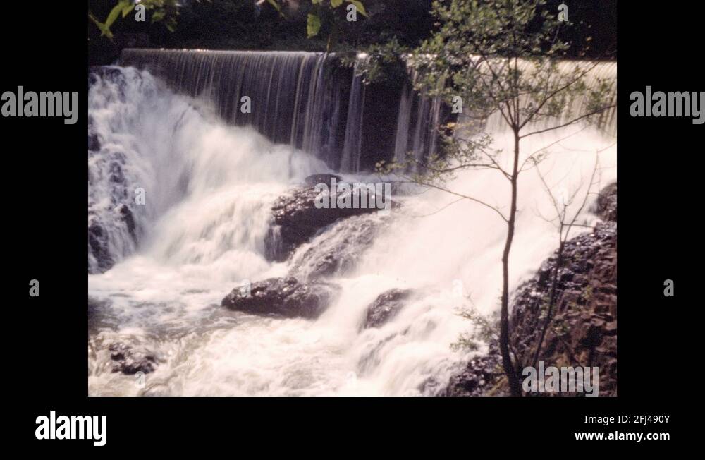 1940s: Water cascades down rocky waterfall; woman leads string of ...