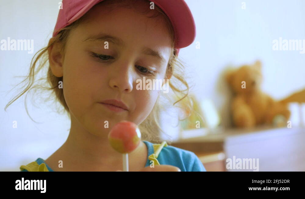Little girl enjoying a lollipop while staring at camera. Child eating ...
