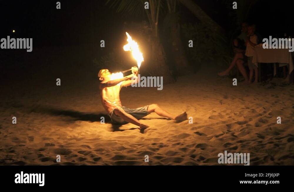 Slowmotion of a fire performer rotating fire while laying on the beach ...