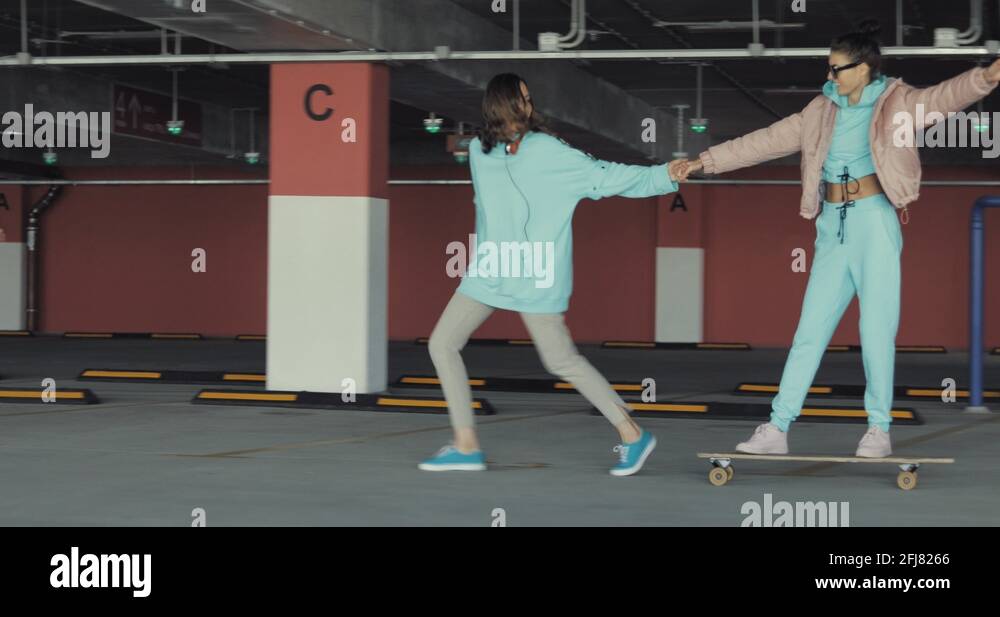 Woman sitting on longboard while her friend pushing her behind Stock ...