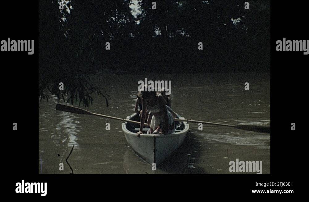 1940s: UNITED STATES: girls row boat to shore. Girl gets out of boat ...