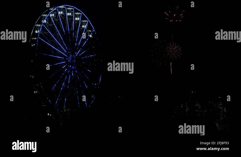 A ferris wheel lights up the sky with a fireworks show beside it in the ...