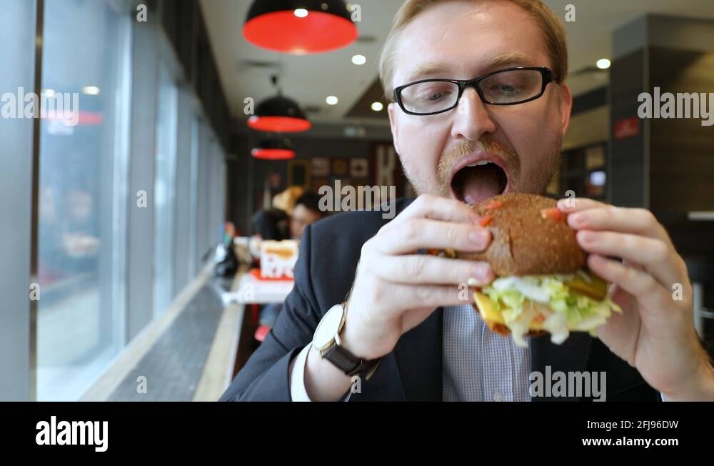 Attractive man with glasses eating Burger in fast food cafe. Slow ...