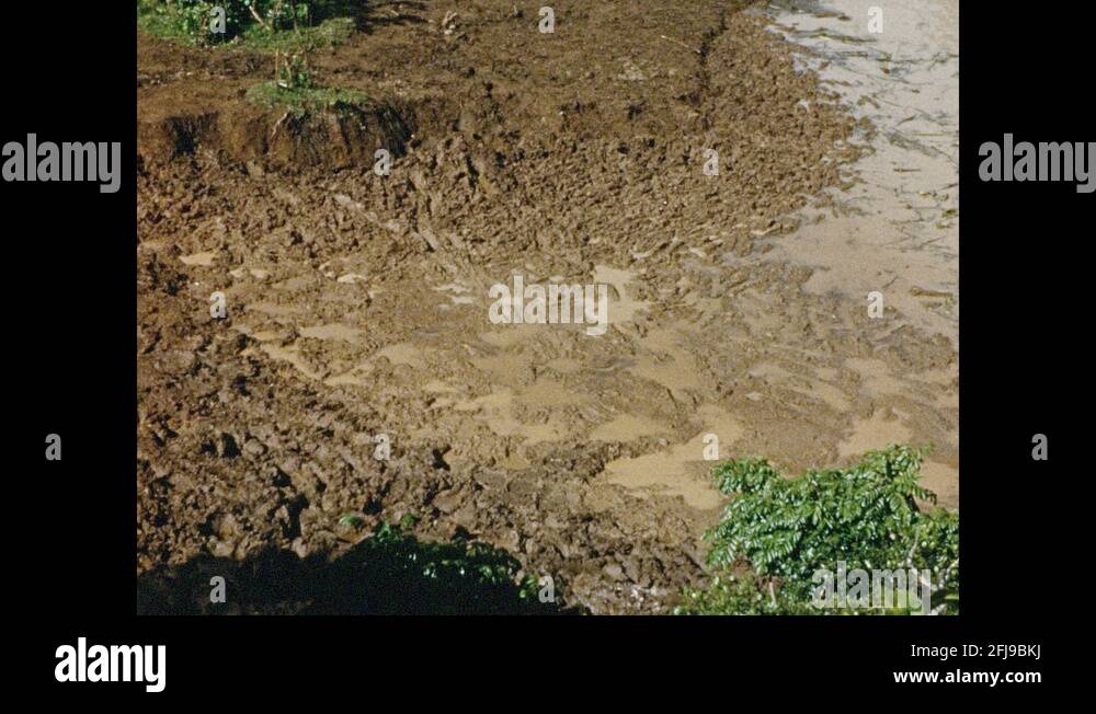 1960s: Muddy water puddle. People lean against handrail on a terrace. A ...