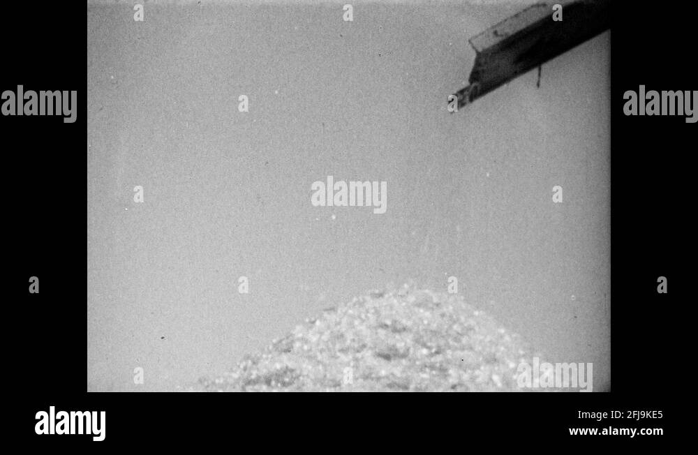 1950s: Broken glass and cullet pour from chute onto large pile. Man ...