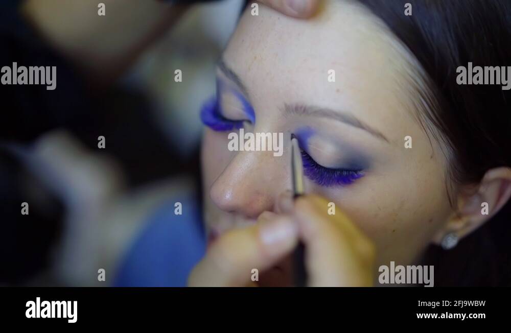 makeup artist is drawing by blue shadows on upper eyelids of young ...