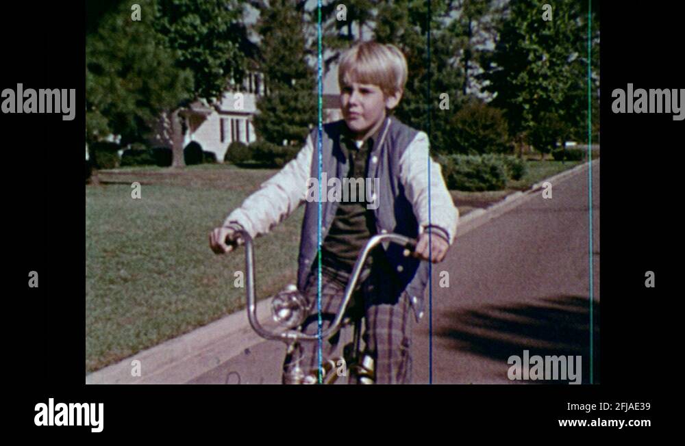 1970s: Boy bicycles down street, signals a left turn, looks behind him ...