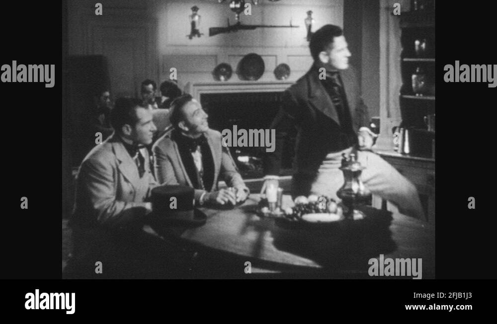 1950s: Three men in 19th century clothes sit around table talking. One ...