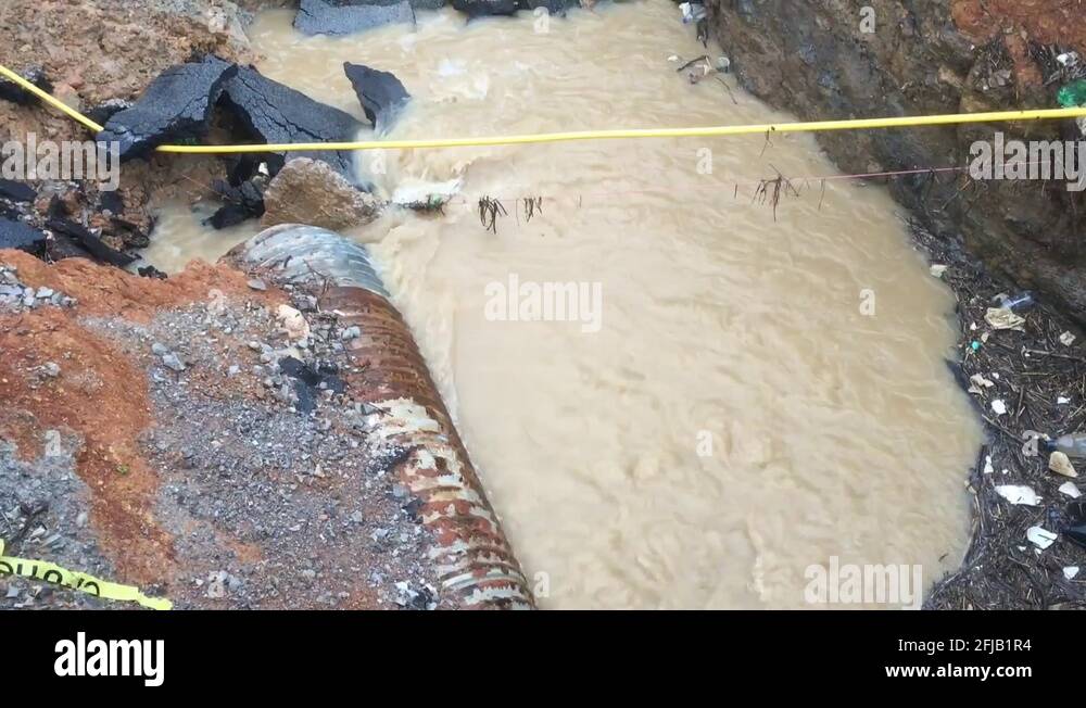 Sinkhole in the middle of the road with a broken culvert with water ...