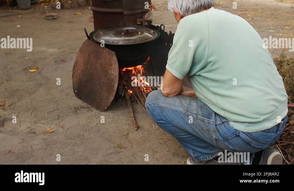 Man Puts Branches In The Fire While Cooking Fish Stew In A Pot Outdoors ...