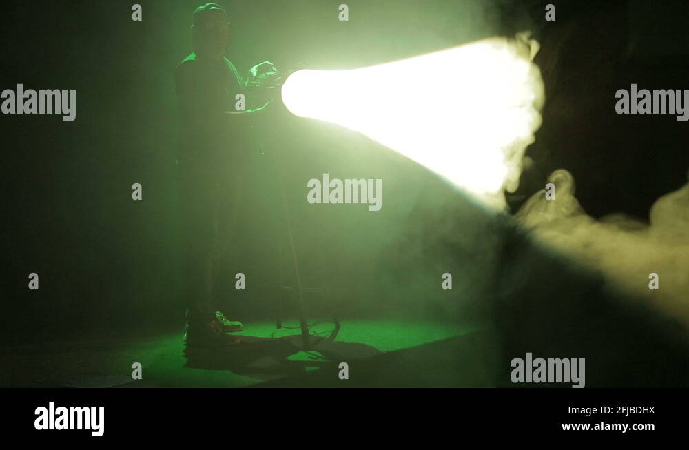A male illuminator directs a beam of light from a profile spotlight and ...